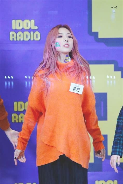 A Woman With Pink Hair And Orange Sweater Standing In Front Of A Purple