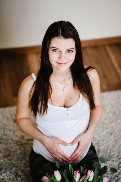 Mulher grávida segurando a barriga um buquê de flores abraçando a