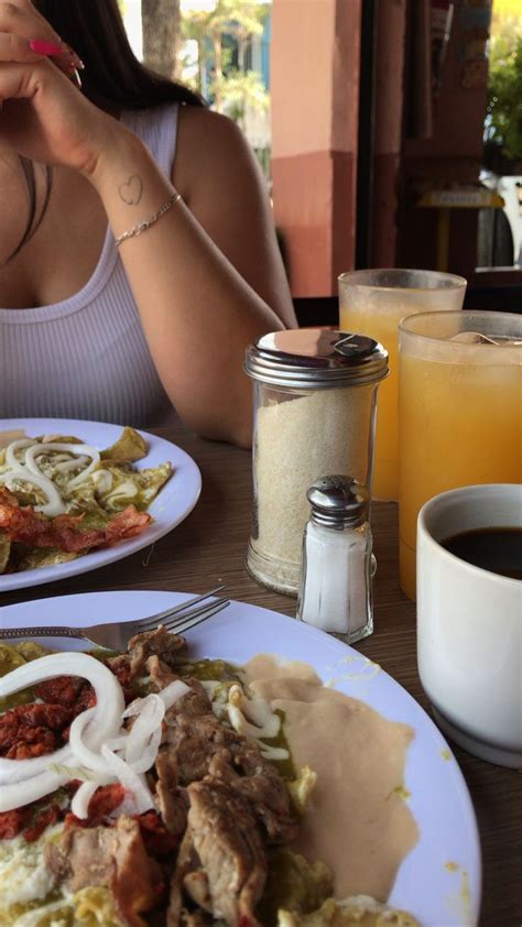 A Woman Sitting At A Table With Two Plates Of Food And Drinks In Front