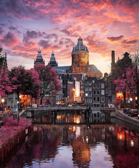 The Sun Is Setting Over An Old City With Pink Flowers On Trees And