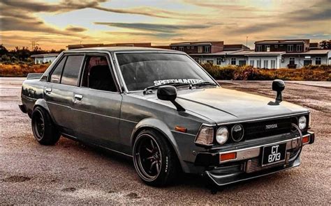 An Old Car Parked In A Parking Lot With The Sun Setting On It S Horizon