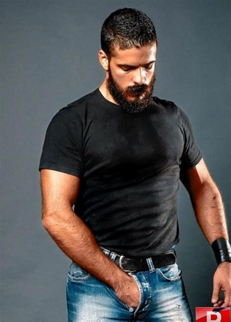 A Man With A Beard And Black Shirt Holding A Red Object In His Hand