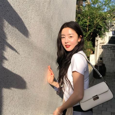A Woman Standing Next To A Wall Holding A White Purse