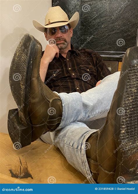 Man Wearing Cowboy Straw Hat And Boots Sitting Down Pondering Feet On