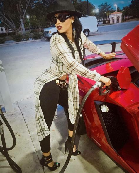 A Woman Sitting On The Hood Of A Red Sports Car With Her Hand On The