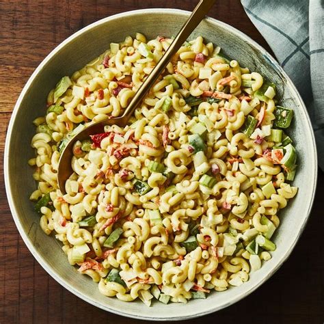 A Bowl Filled With Macaroni Salad On Top Of A Wooden Table Next To A Spoon