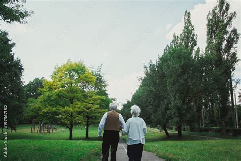Old Couple Is Walking Away In The Green Park Grandmother And Grandfather At Their Golden
