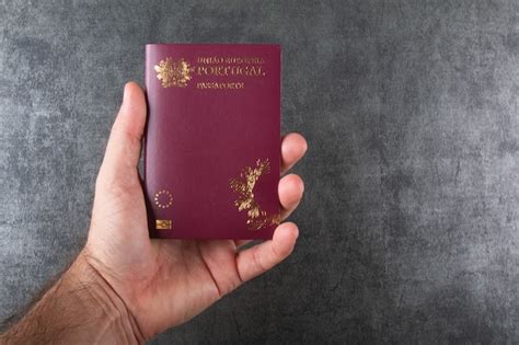 Mão segurando o passaporte português fundo cinza Foto Premium